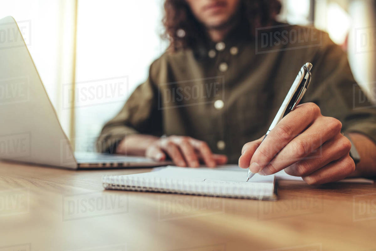 Businessman writing in notepad with a laptop on the desk. Close up of ...