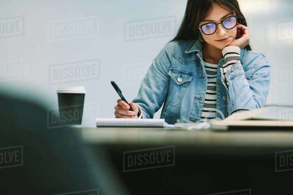 Happy female student sitting at college library and making notes. Woman ...
