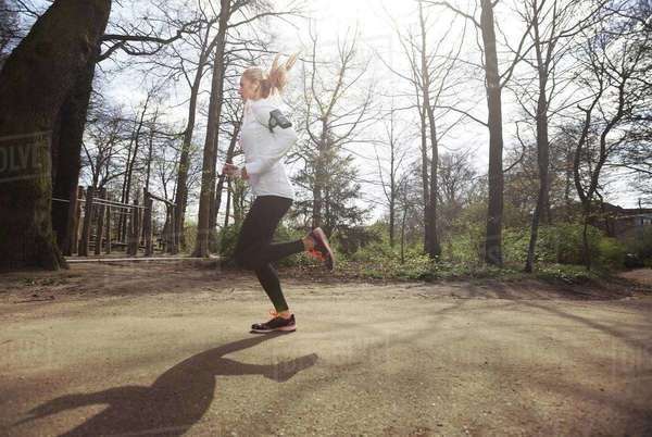 Side view of caucasian female runner running outdoors in forest ...