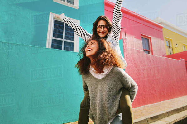 Young woman carrying her female friend on her back. Two young woman ...