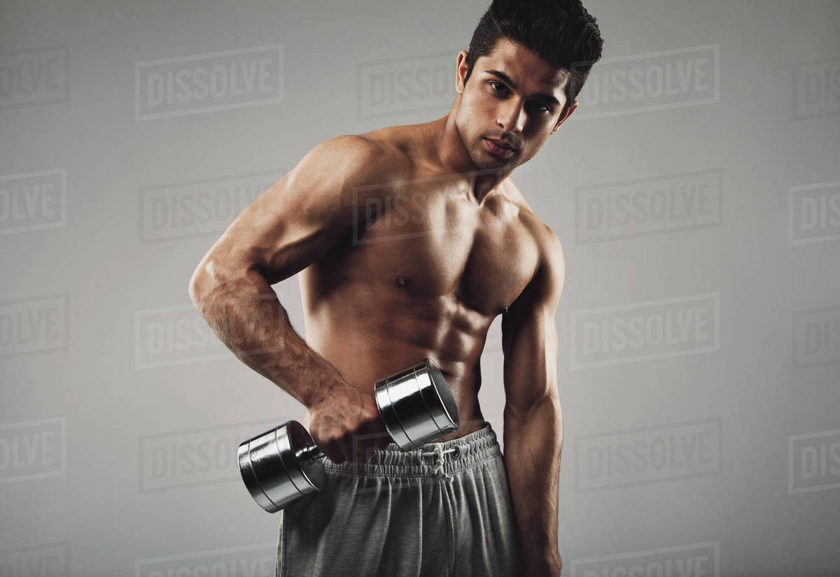 Portrait of hispanic young man working out with heavy dumbbell on grey ...