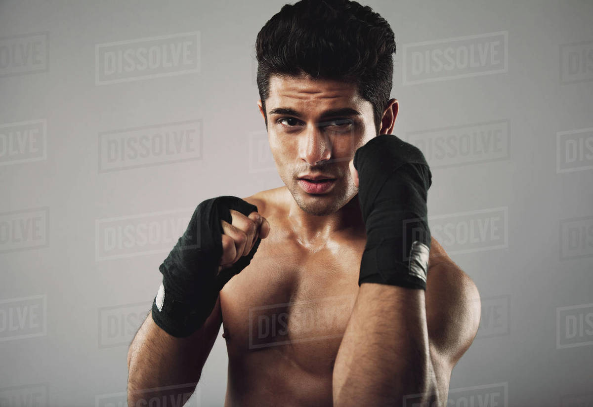 Portrait of strong young man wearing boxing gloves practicing shadow ...