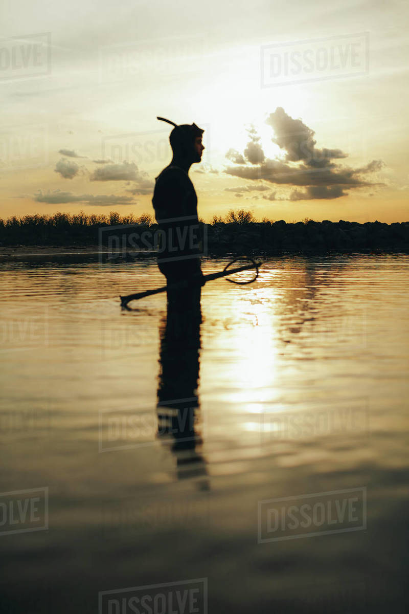 Side view of a male diver standing in water. Spear fisherman with ...
