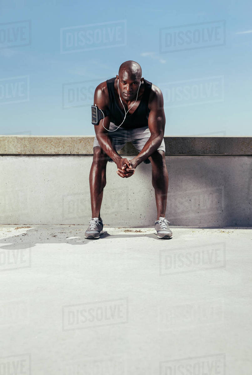 Portrait of a exhausted runner sitting outdoors. Muscular and fit young ...