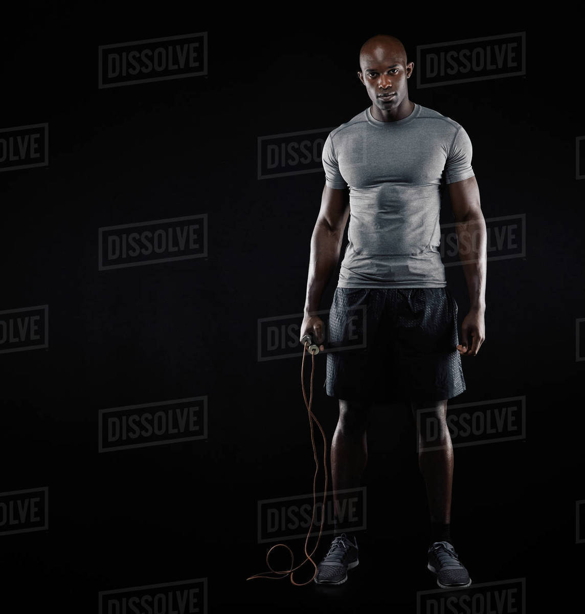 Studio shot of fit and muscular man with jumping rope standing on black ...