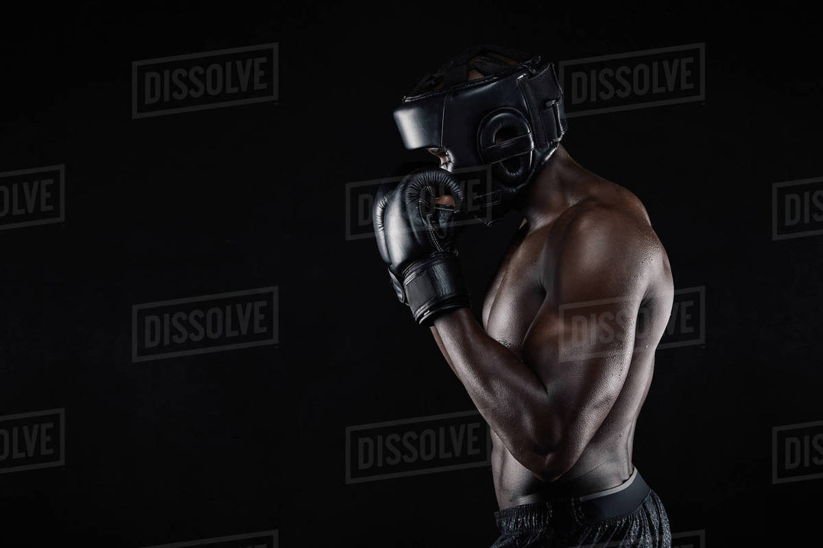 Side view of a young male boxer in a fighting stance on black ...