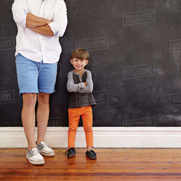 Indoor shot of little boy standing next to his father with hands folded ...