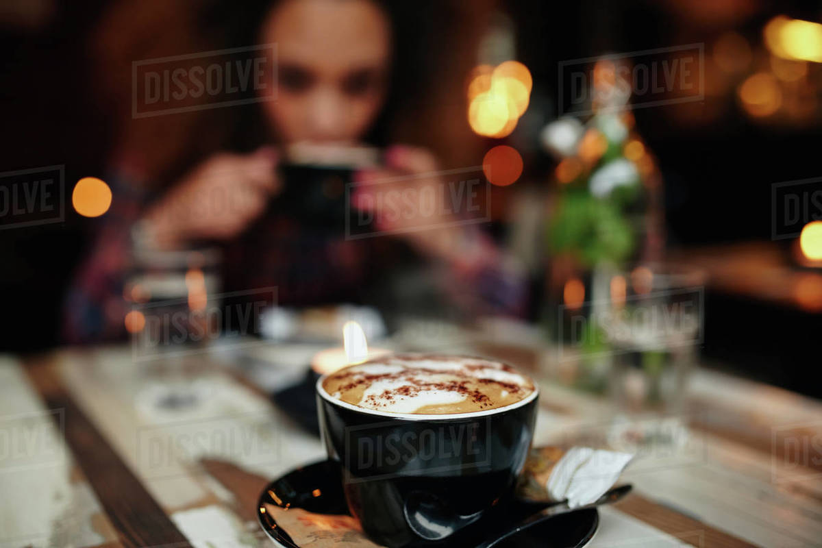 Close up shot of cup of coffee on table at cafe, with a woman drinking ...