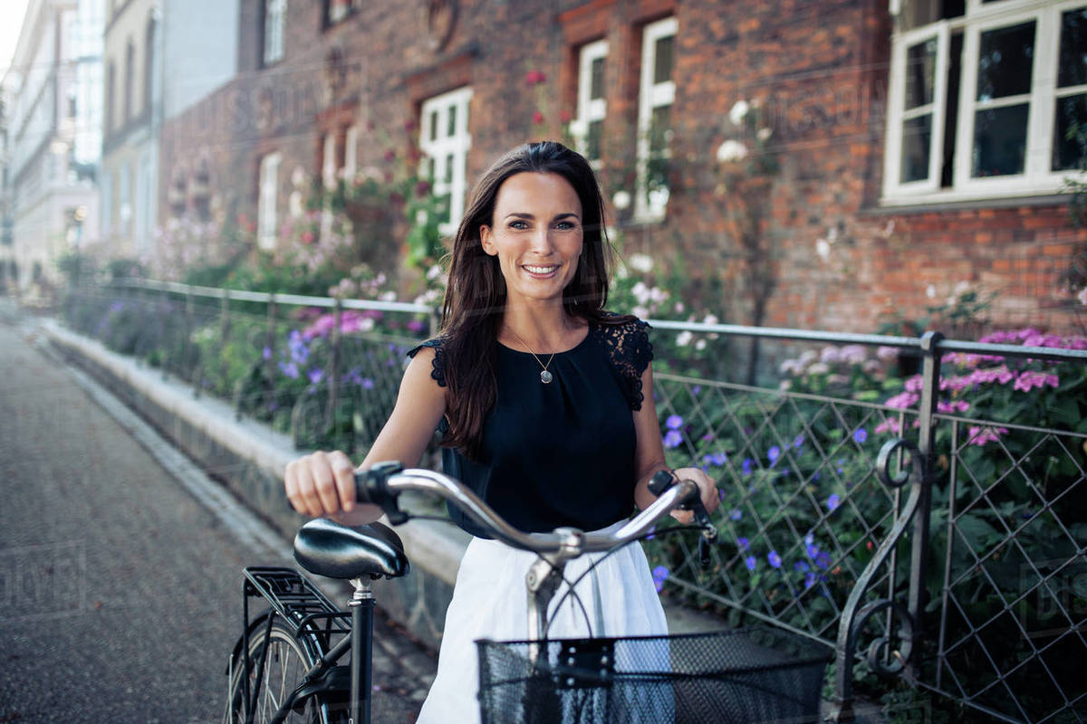 Beautiful woman with a cycle walking down the city road. Caucasian ...
