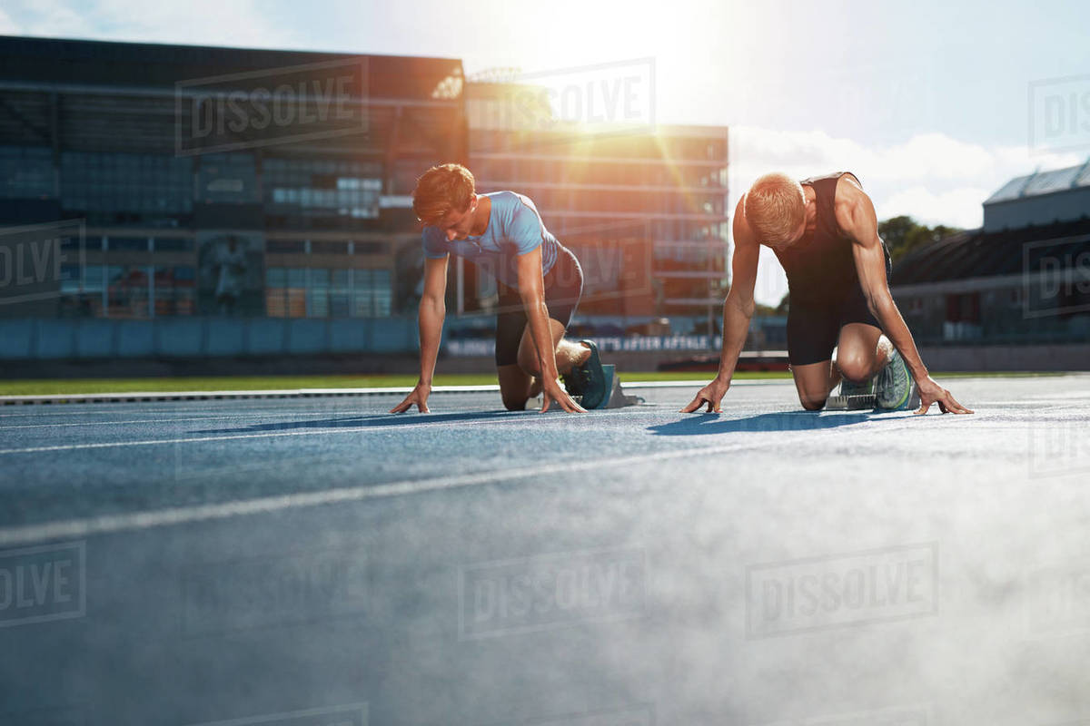 Young athletes preparing to race in start blocks in stadium. Sprinters ...