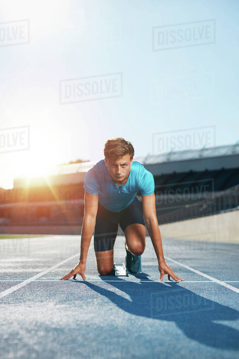 Vertical shot of young male runner taking ready to start position ...