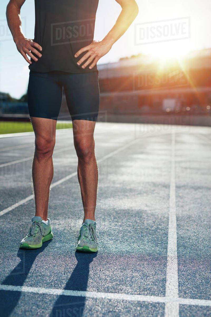 Low section shot of athlete man standing on race track with his hands ...