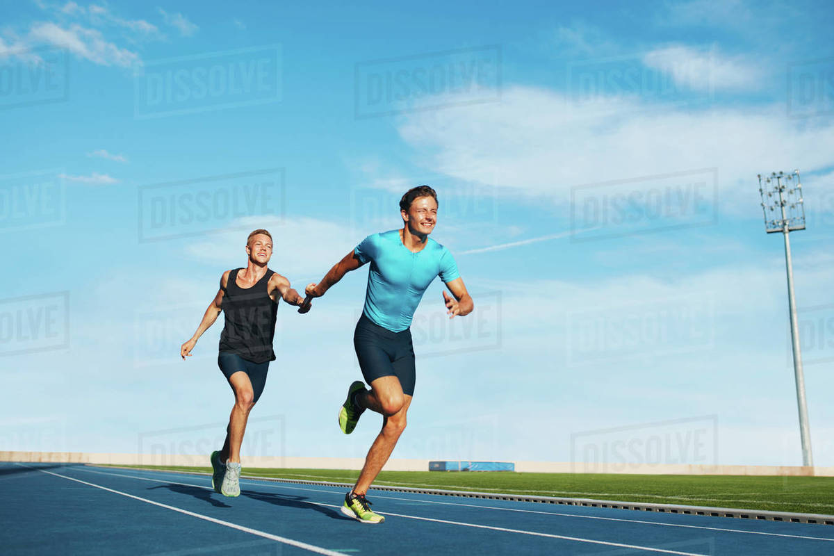 Shot of professional male athletes passing over the baton while running ...