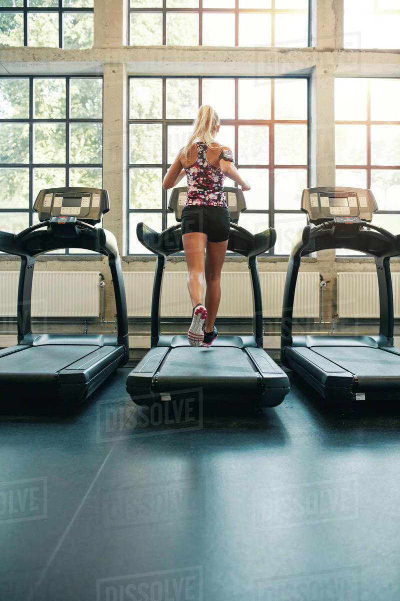 Rear view of young female running on treadmill in gym. Fitness woman ...