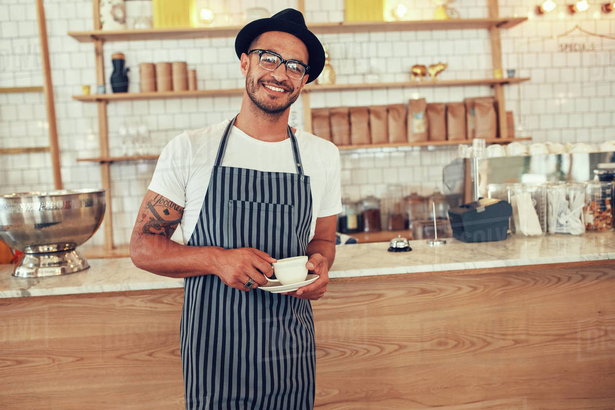 Portrait of happy young barista at work. Caucasian man wearing apron ...