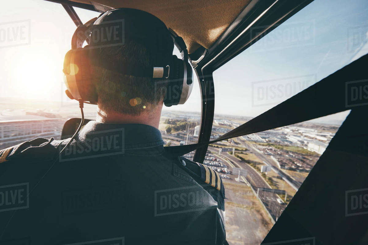 Rear view of a male wearing headphones flying a helicopter. Pilot ...