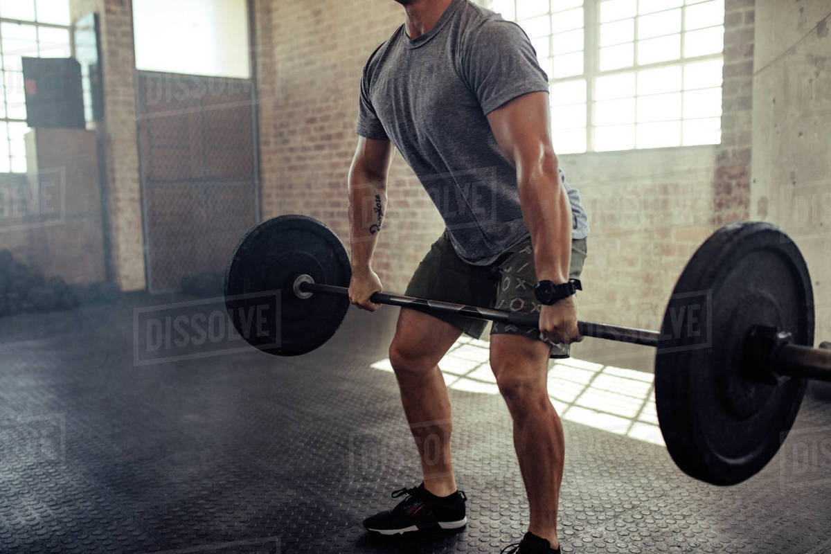 Cropped image of muscular young man lifting barbell at gym. Fit man ...