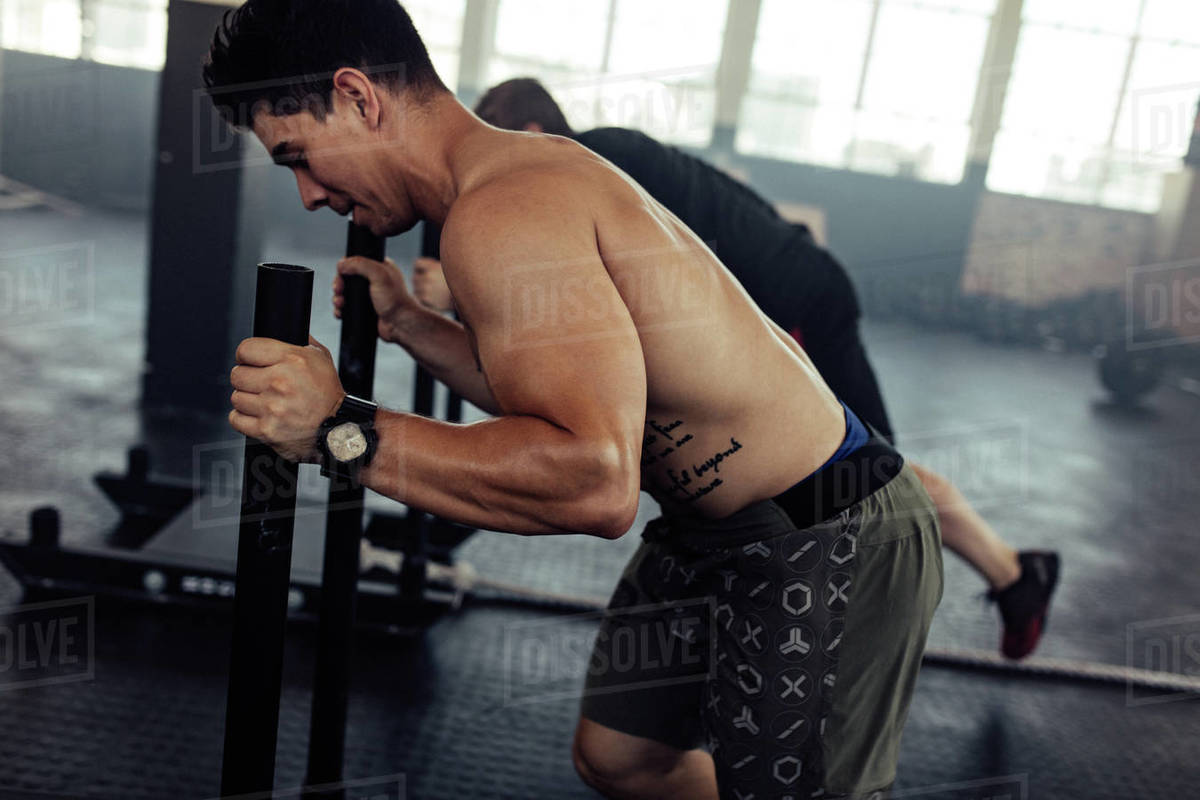 Side portrait of young muscular men pushing prowler sled at crossfit ...