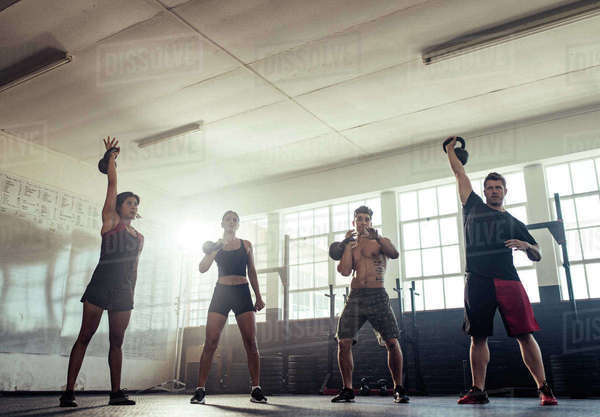 Full length portrait of fit young people exercising with kettle bell ...