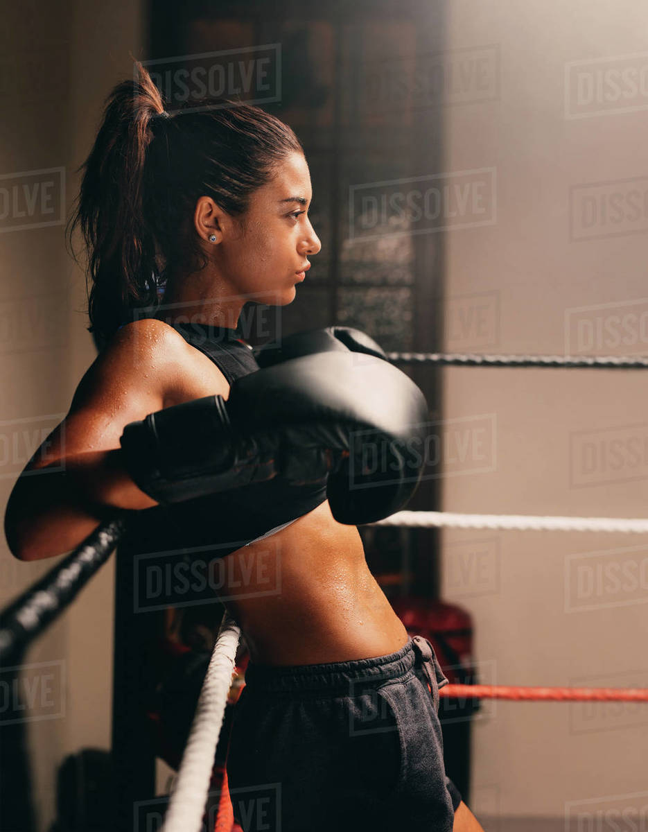 Young muscular female boxer leans against ropes in boxing ring with her ...