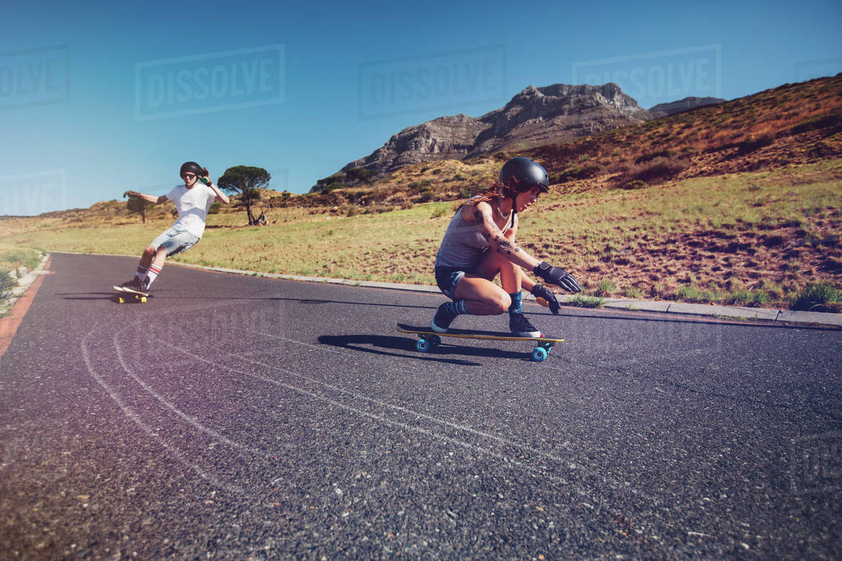 Two young people practicing long board riding outdoors on rural road ...