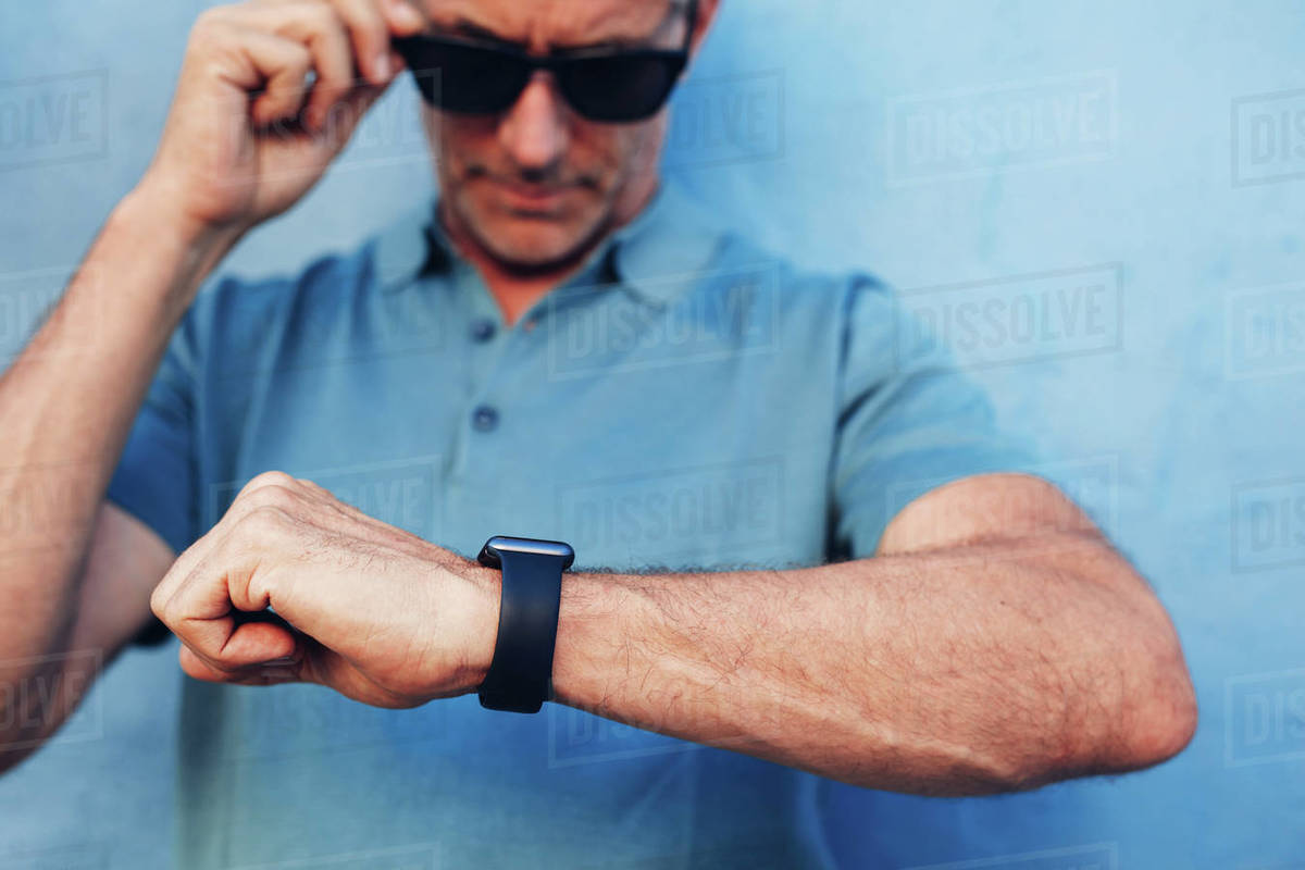 Portrait of mature man checking time on his wristwatch against blue ...