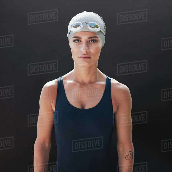 Portrait of young woman in swimwear standing on black background ...