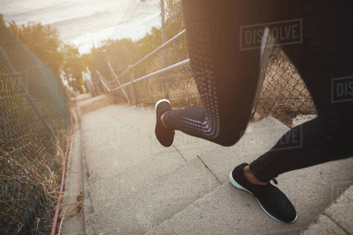 Close up shot of female runner running up steps for exercise. Focus on ...
