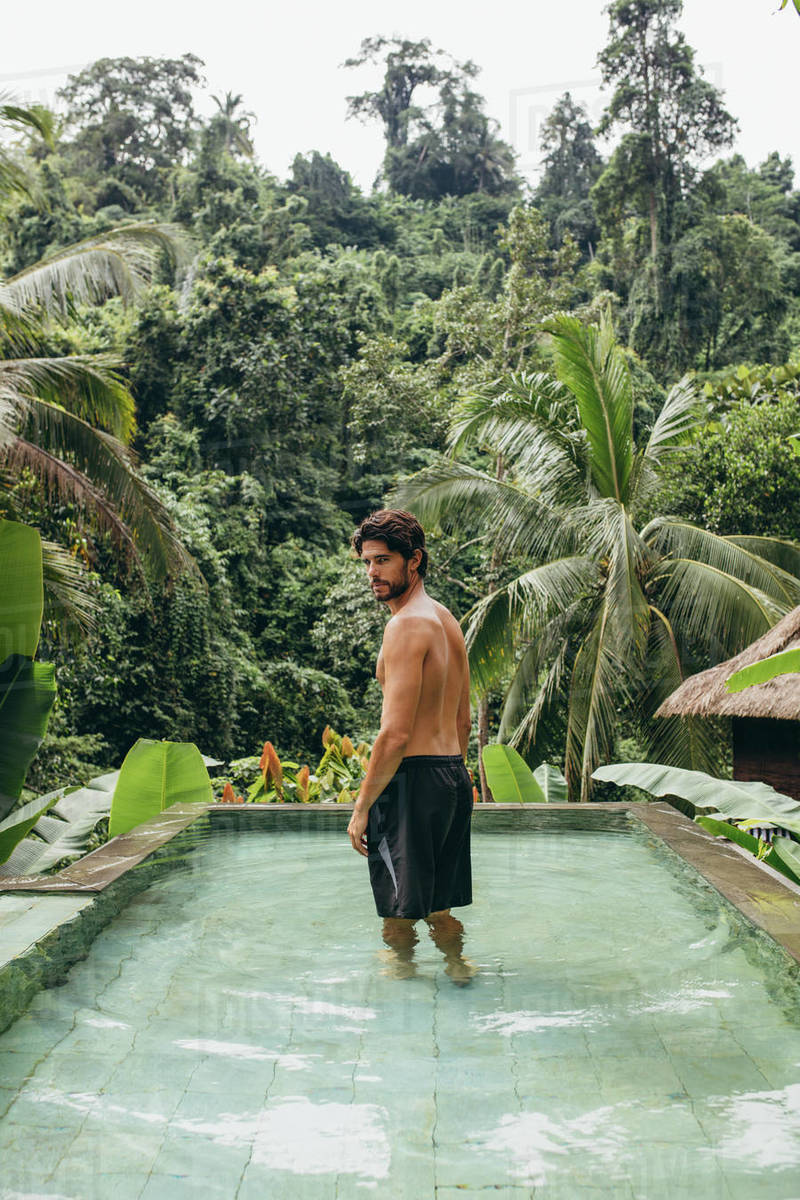 Outdoor shot of young male standing in pool and looking over shoulder ...