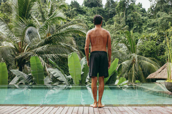 Rear view shot of young man standing on the edge of the pool. Male in ...