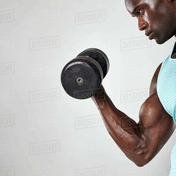 Side view shot of young and muscular african man doing biceps curl with ...