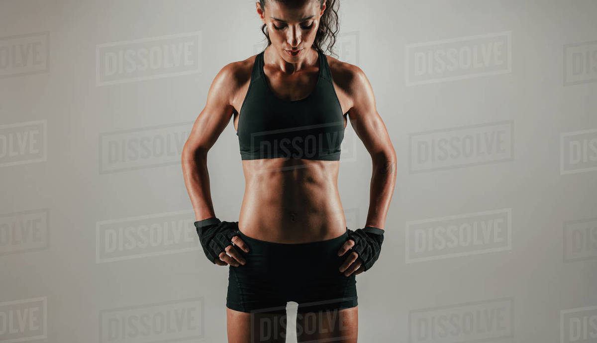Trim abdominal muscles of woman with gloved hands on hips over gray ...
