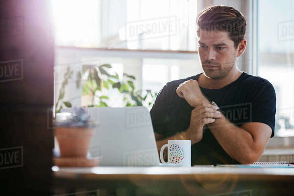 Shot of young man sitting at his desk and looking at a laptop ...