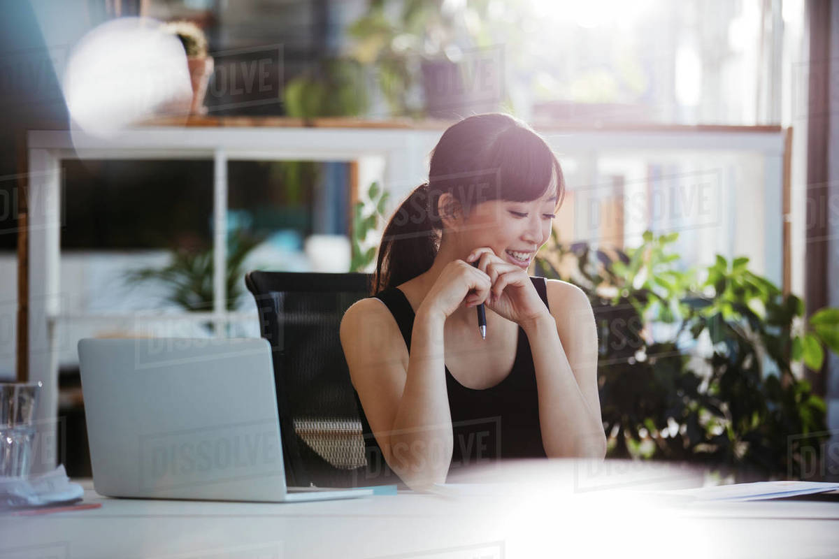 Shot of young woman sitting at office desk looking at documents and ...