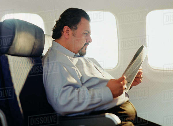 Overweight man reading newspaper on airplane - Stock Photo - Dissolve