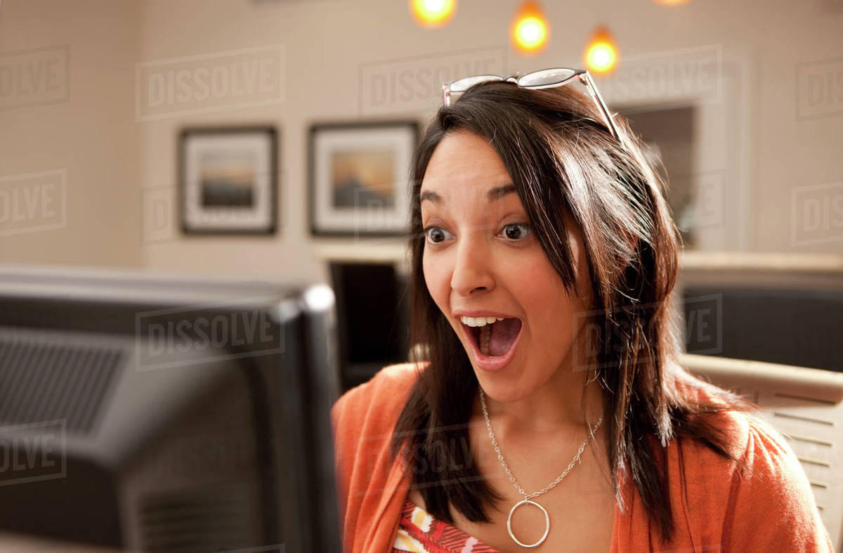Surprised Hispanic woman using computer - Stock Photo - Dissolve