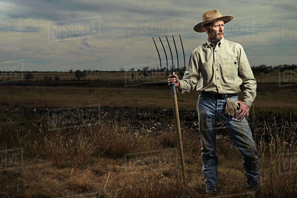 Farmer standing with pitchfork in field - Stock Photo - Dissolve
