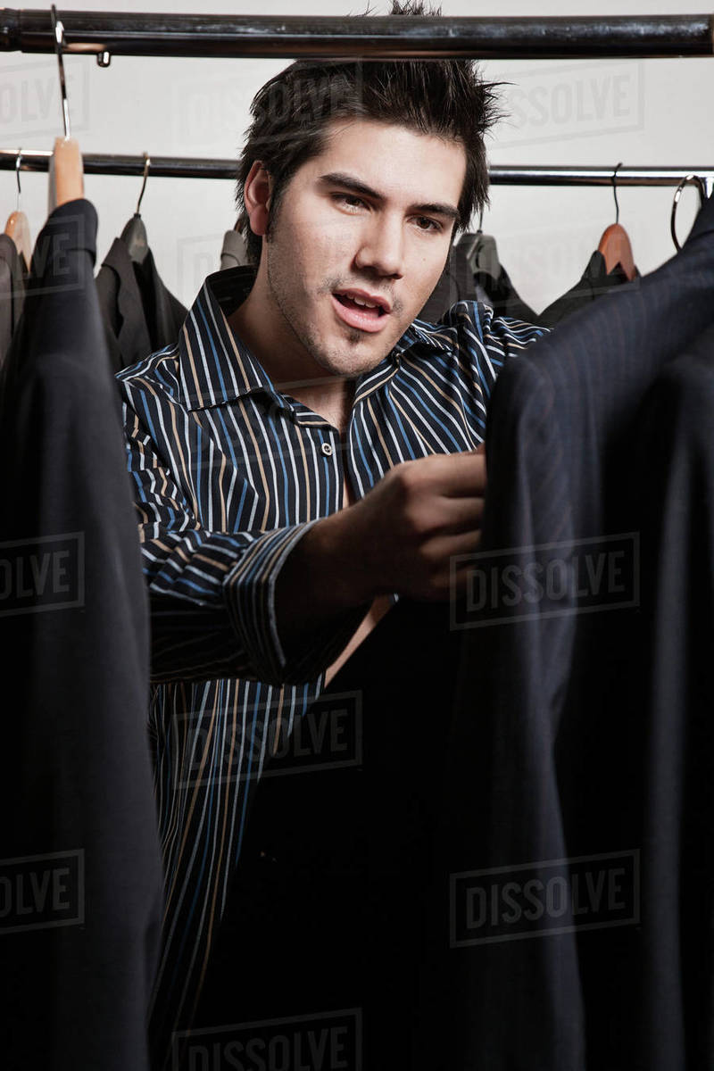 Hispanic man examining rack of suits - Royalty-free Stock Photo | Dissolve