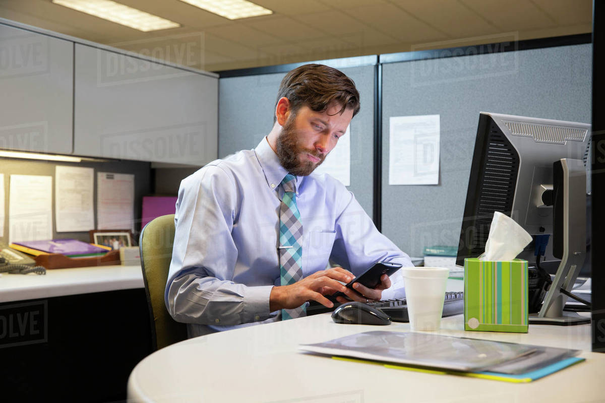 Young Caucasian man working in cubicle at office, fighting off a cold ...