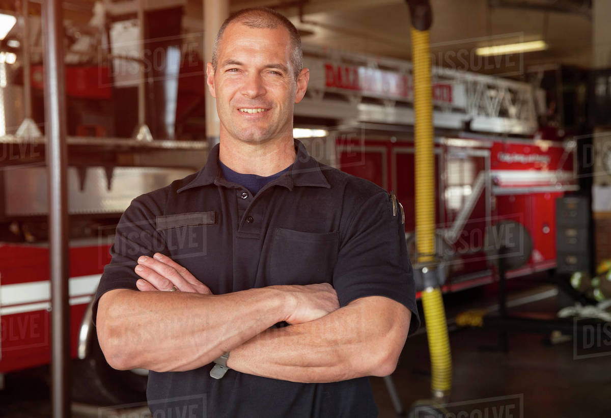 Portrait of Fireman standing in front of firetruck with arms crossed ...
