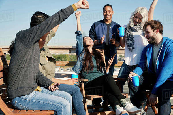 Group of young co-workers hanging out on rooftop patio having a drink ...