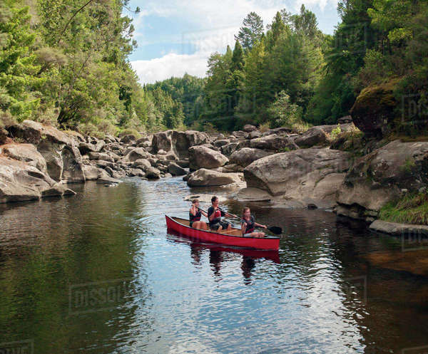 Three young adults in a canoe rowing in river in the wilderness - Stock ...