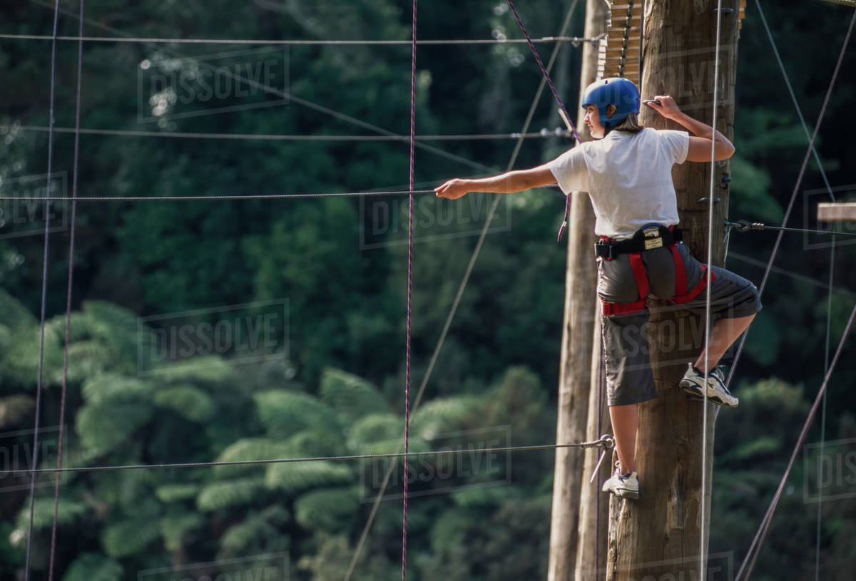 Woman standing at top of post ready to balance on suspended rope at ...