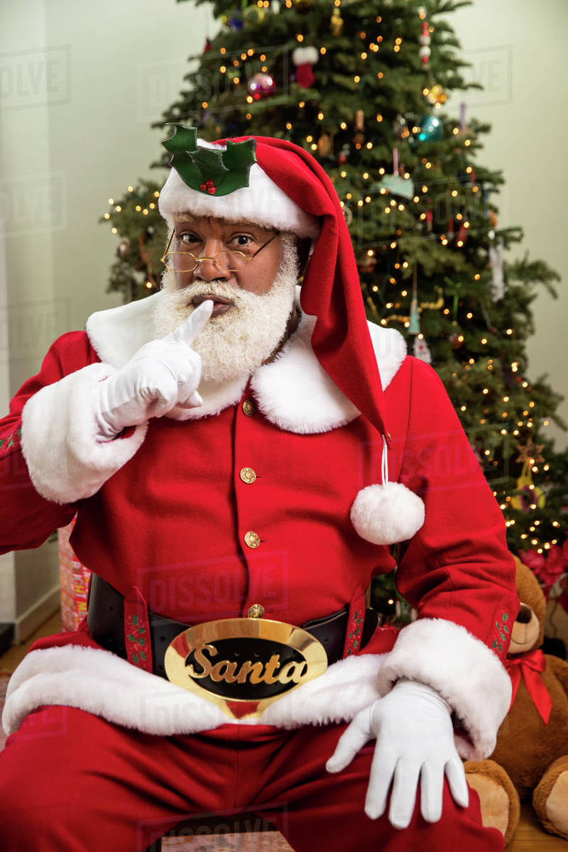 A Black Santa Claus looking into camera and making a shushing gesture ...