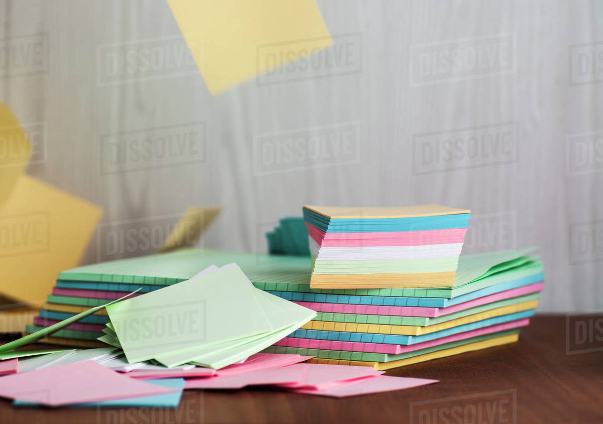 Different coloured note paper and pads stacked on wooden desk and ...