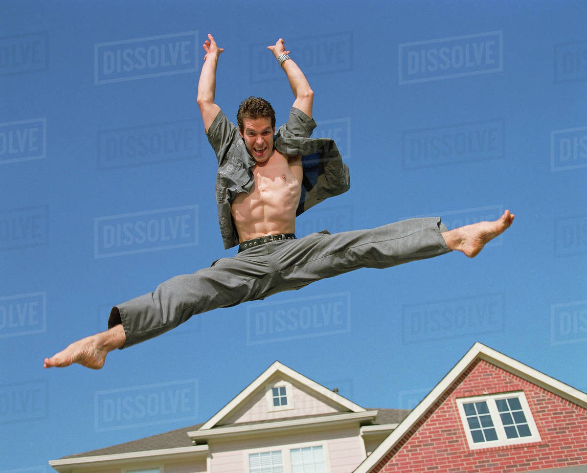Young man jumping in front of home, striking a pose mid air - Royalty ...