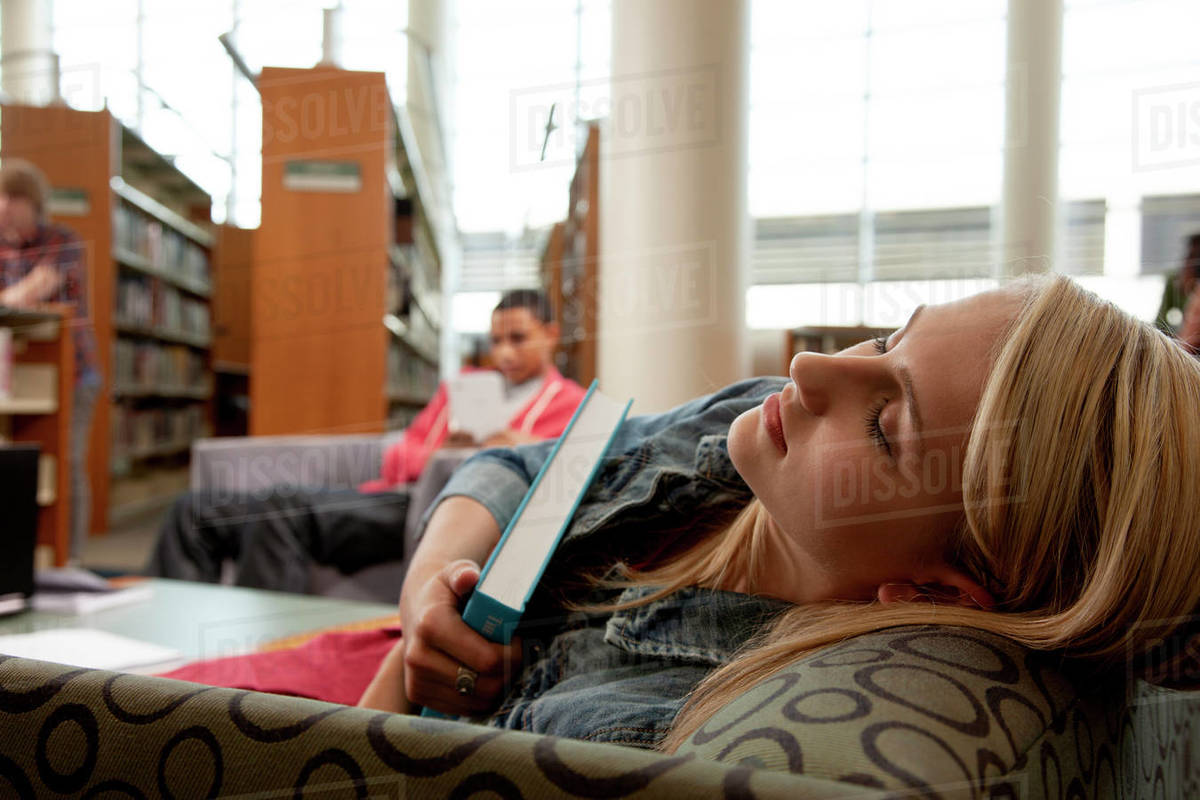 College girl sleeping in library with textbook in hands, exhausted ...