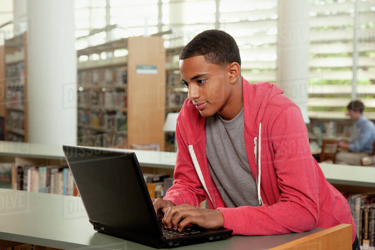 Black college student with laptop studying in library using laptop ...
