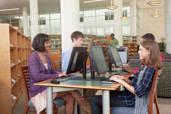 Group of diverse students working on computers in public library ...