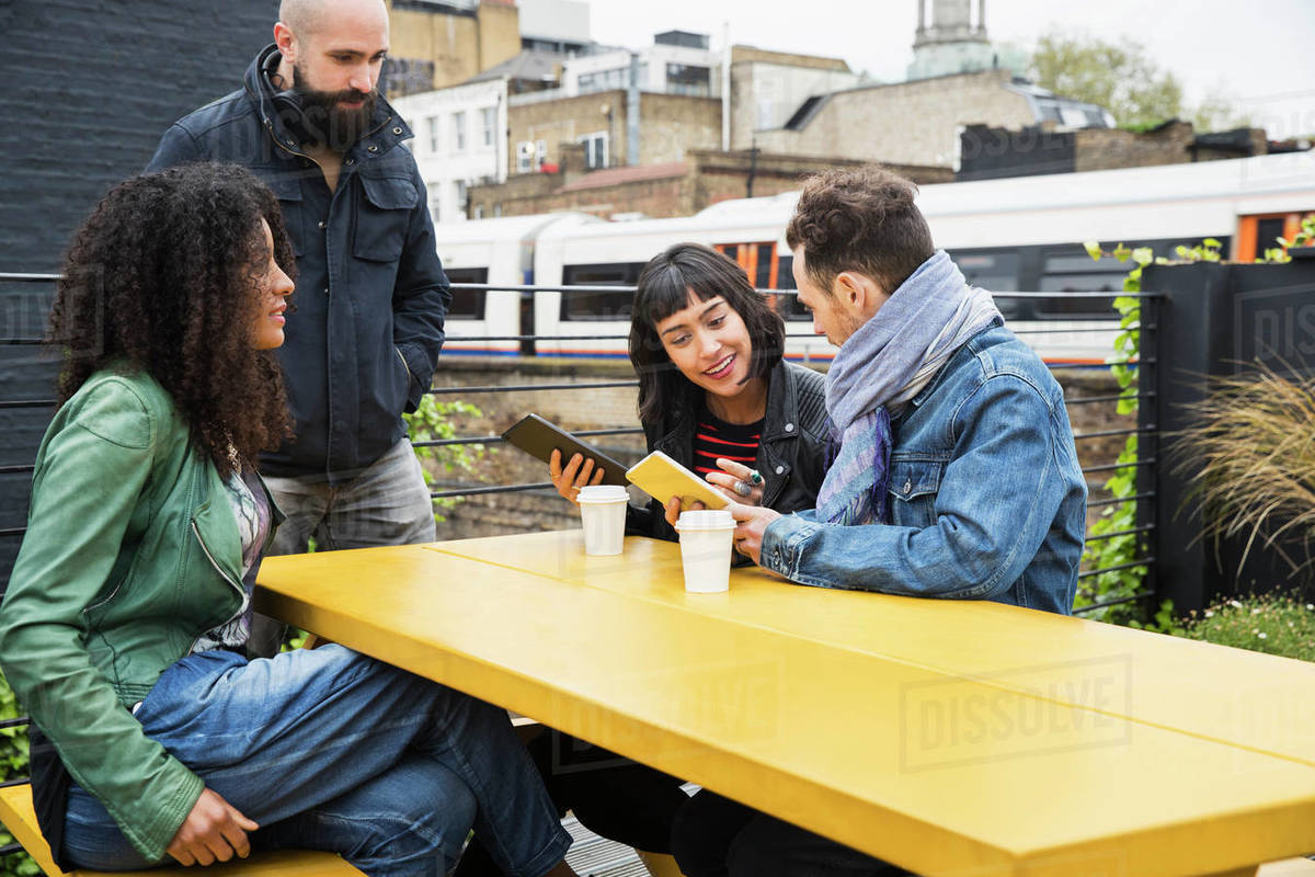 Group of friends working on tablets at outdoor patio table in co ...